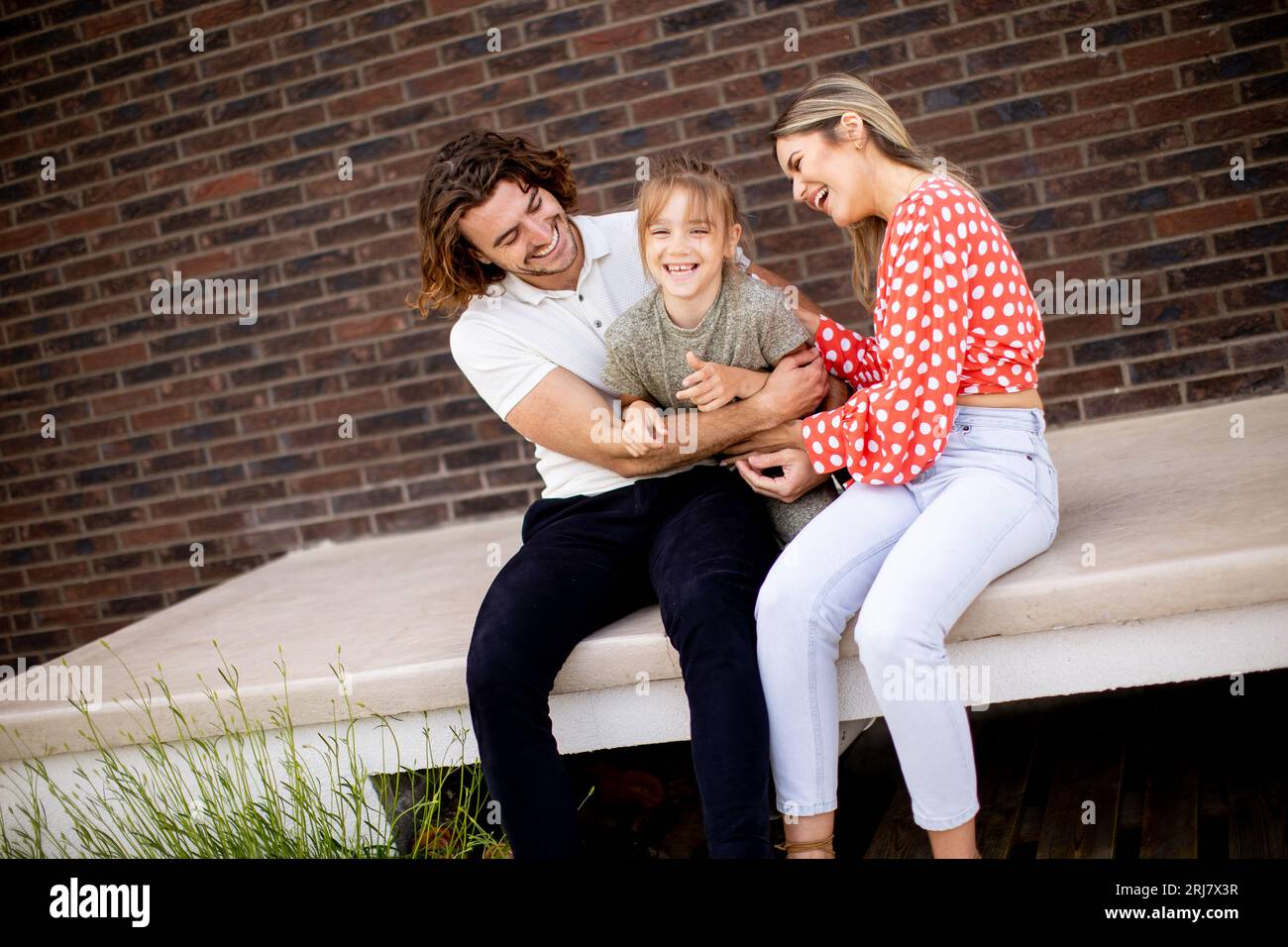 Family with a mother, father and daughter sitting outside on steps of a ...