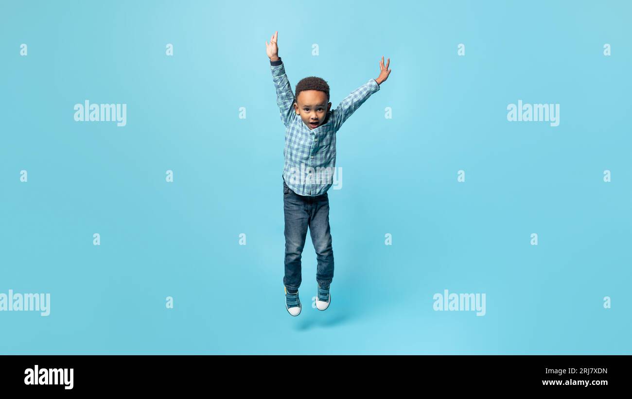 Playful african american little boy jumping with hands up, blue ...