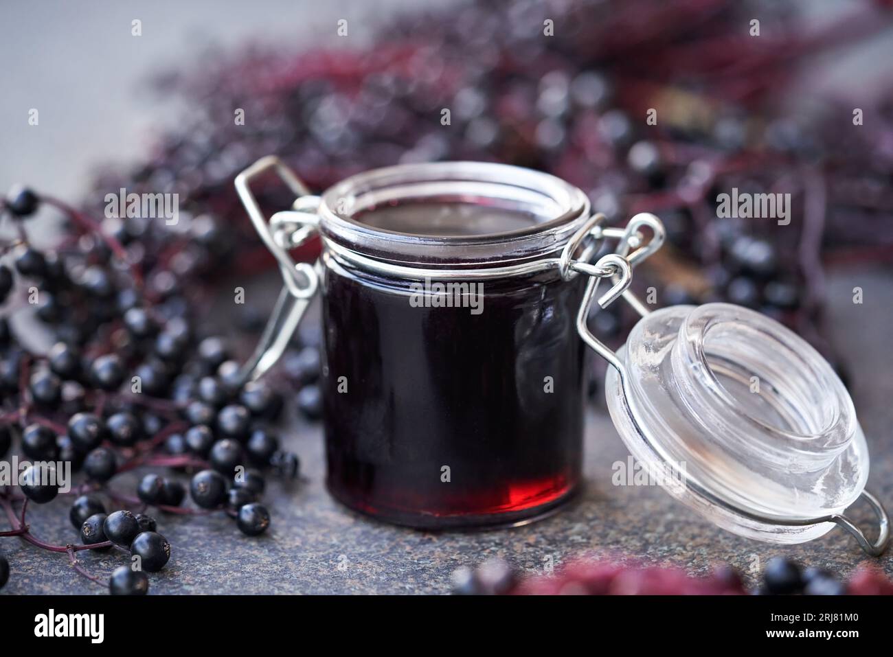 Homemade black elder syrup in a jar with fresh elderberries in the ...