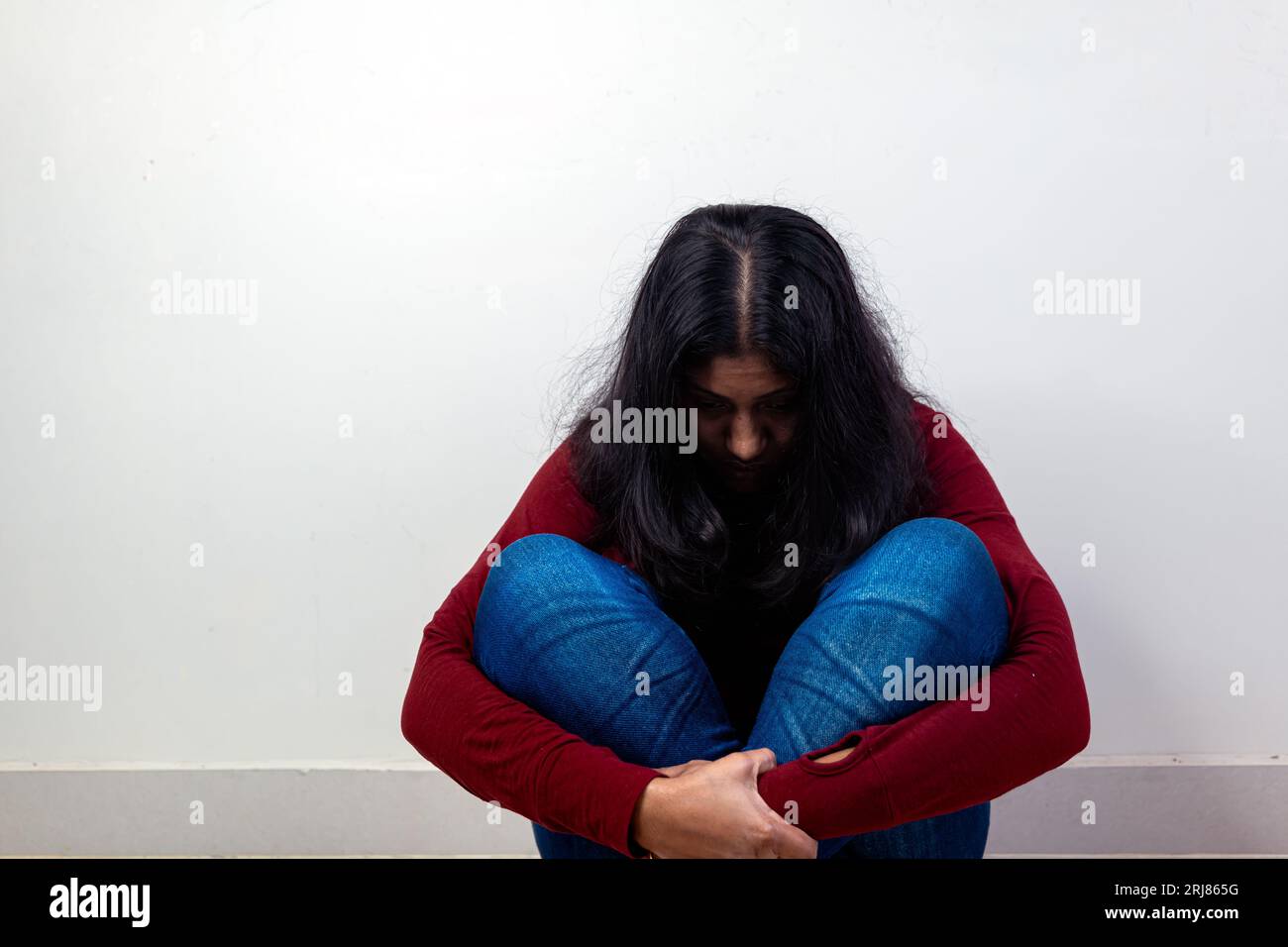 A close-up of a sad woman looking down, her face obscured by her hair ...