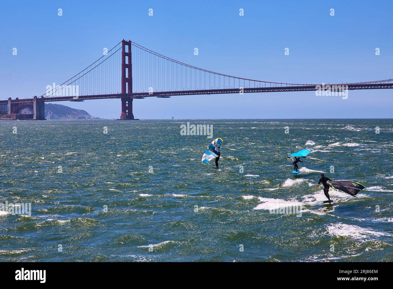 Three people sailboarding on choppy bay waters with Golden Gate Bridge ...