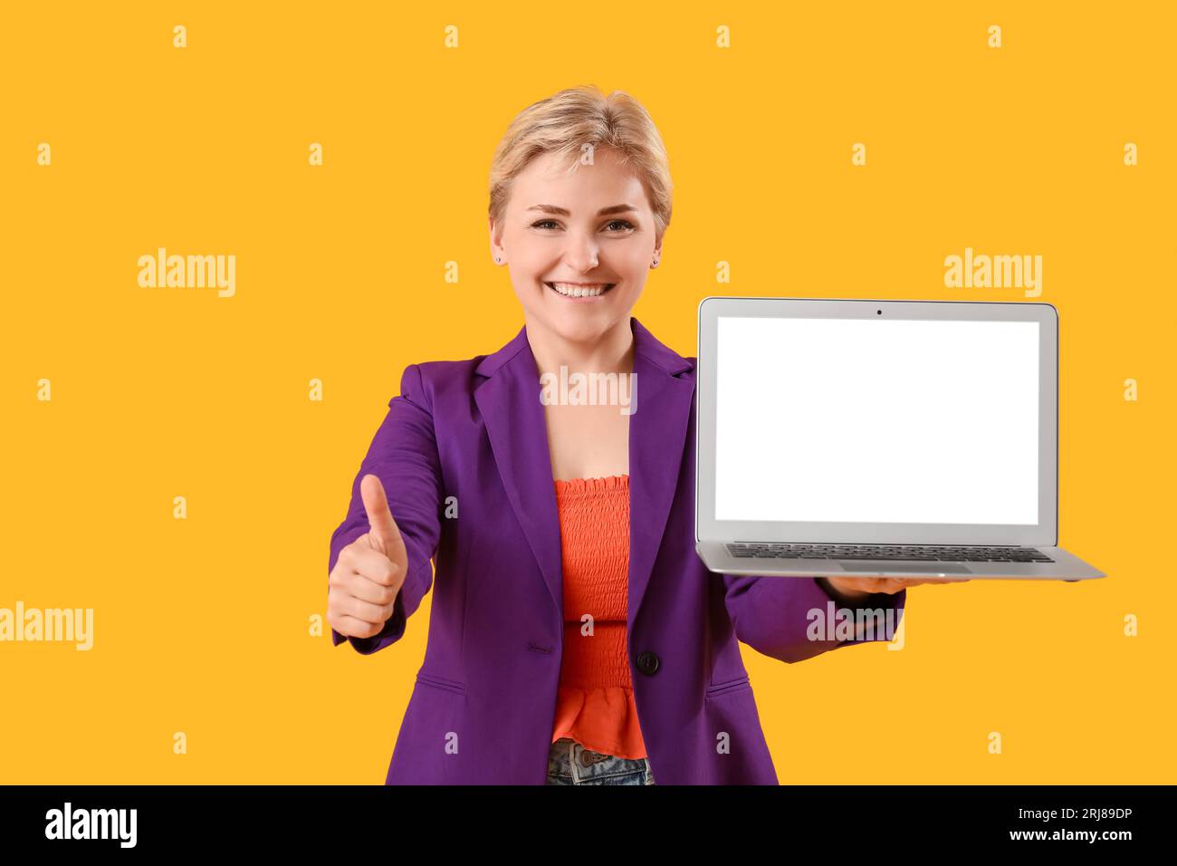 Happy young female programmer with laptop showing thumb-up gesture on yellow background Stock ...