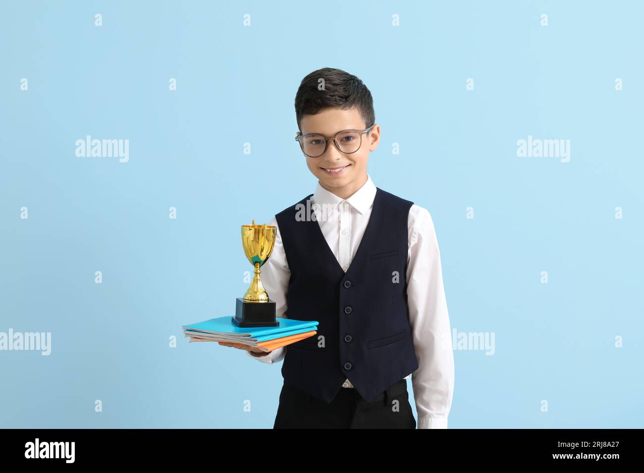 Smart little school boy with prize cup and copybooks on light blue ...