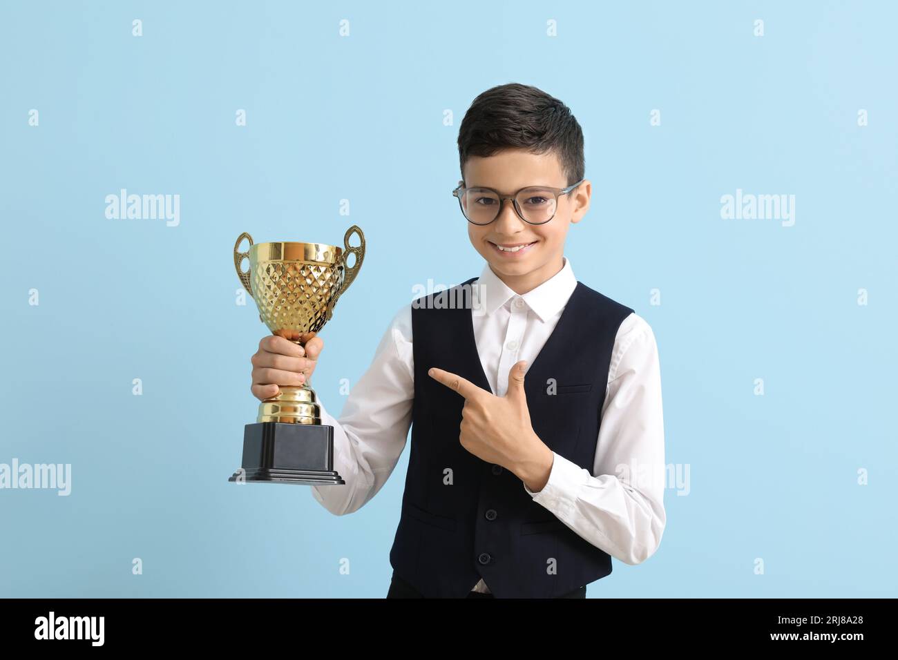 Smart little school boy with prize cup on light blue background Stock ...