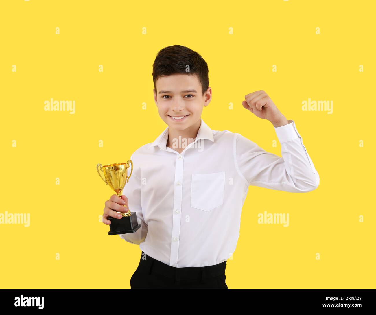 Smart little school boy with prize cup on yellow background Stock Photo ...