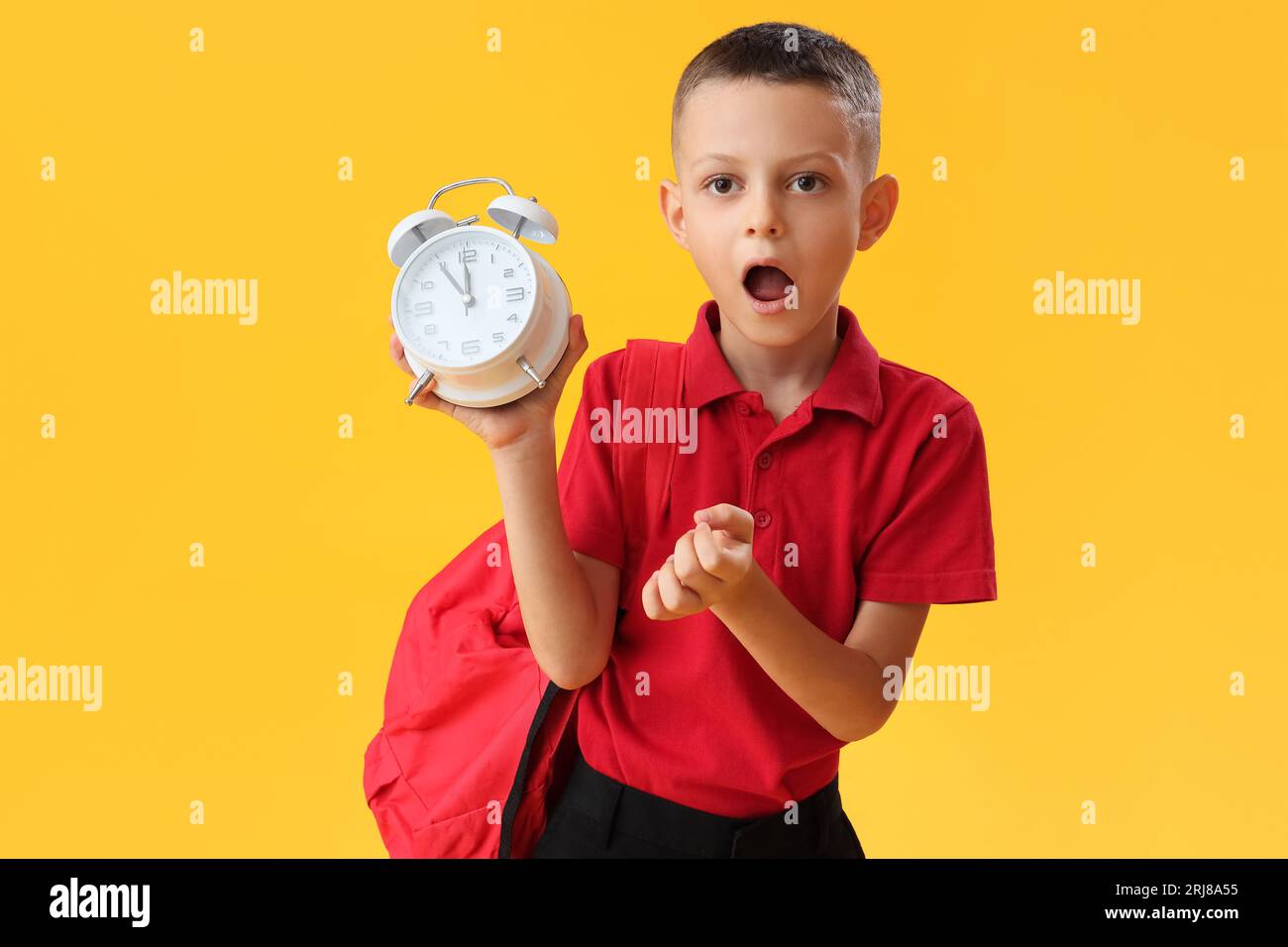 Surprised school boy with alarm clock on yellow background Stock Photo ...