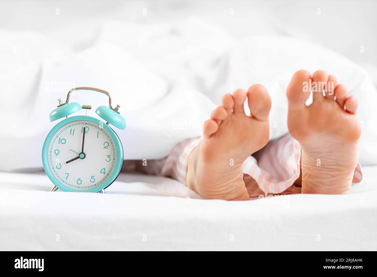 Sleeping woman's feet with alarm clock in bed, closeup Stock Photo - Alamy