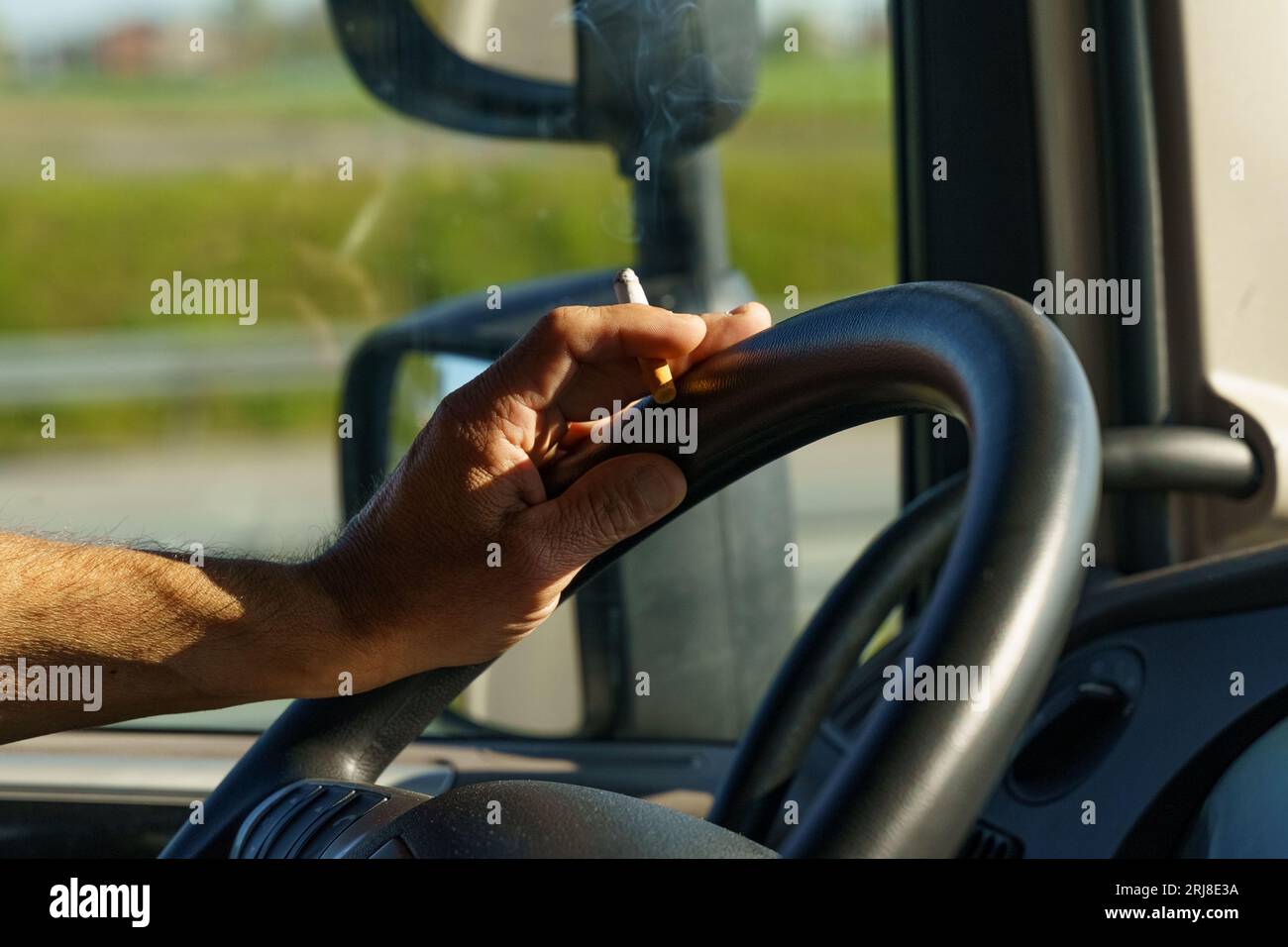 The truck driver holds a smoldering cigarette in his hands and controls ...
