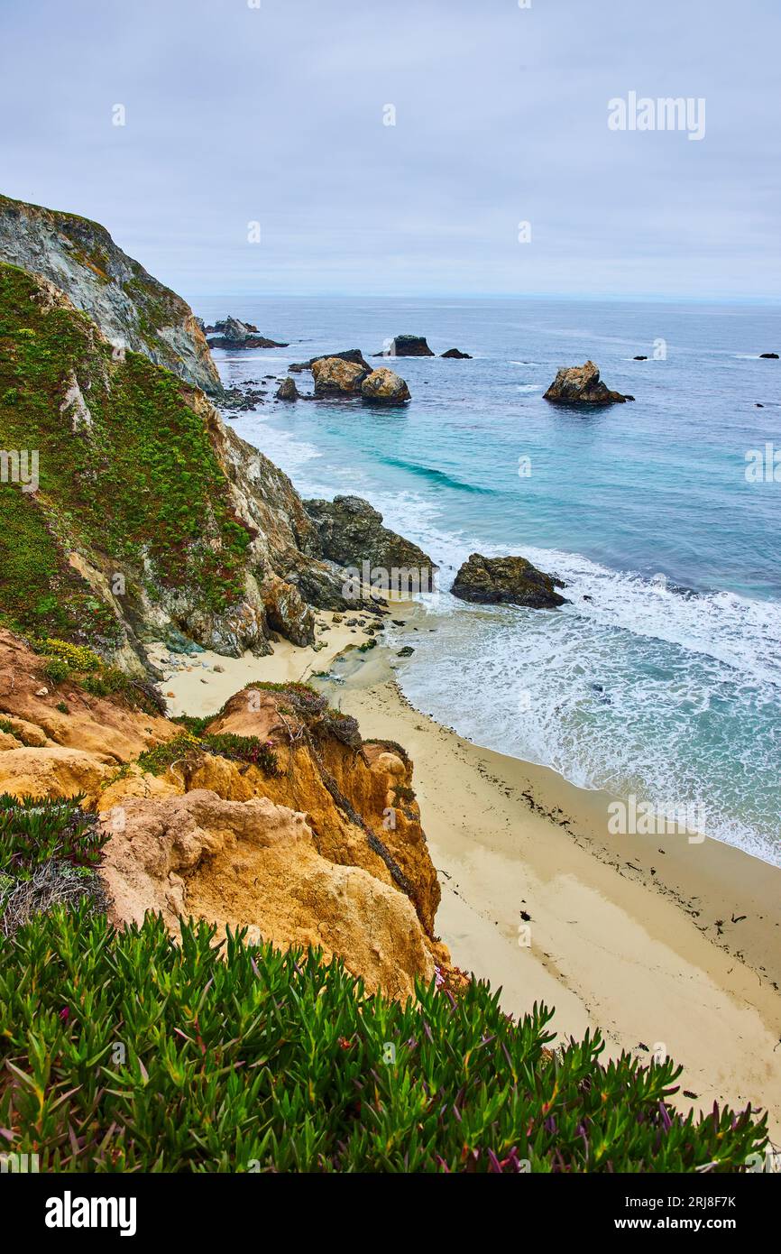 Scenic green cliffy hillside with sandy shore below and ocean waves ...