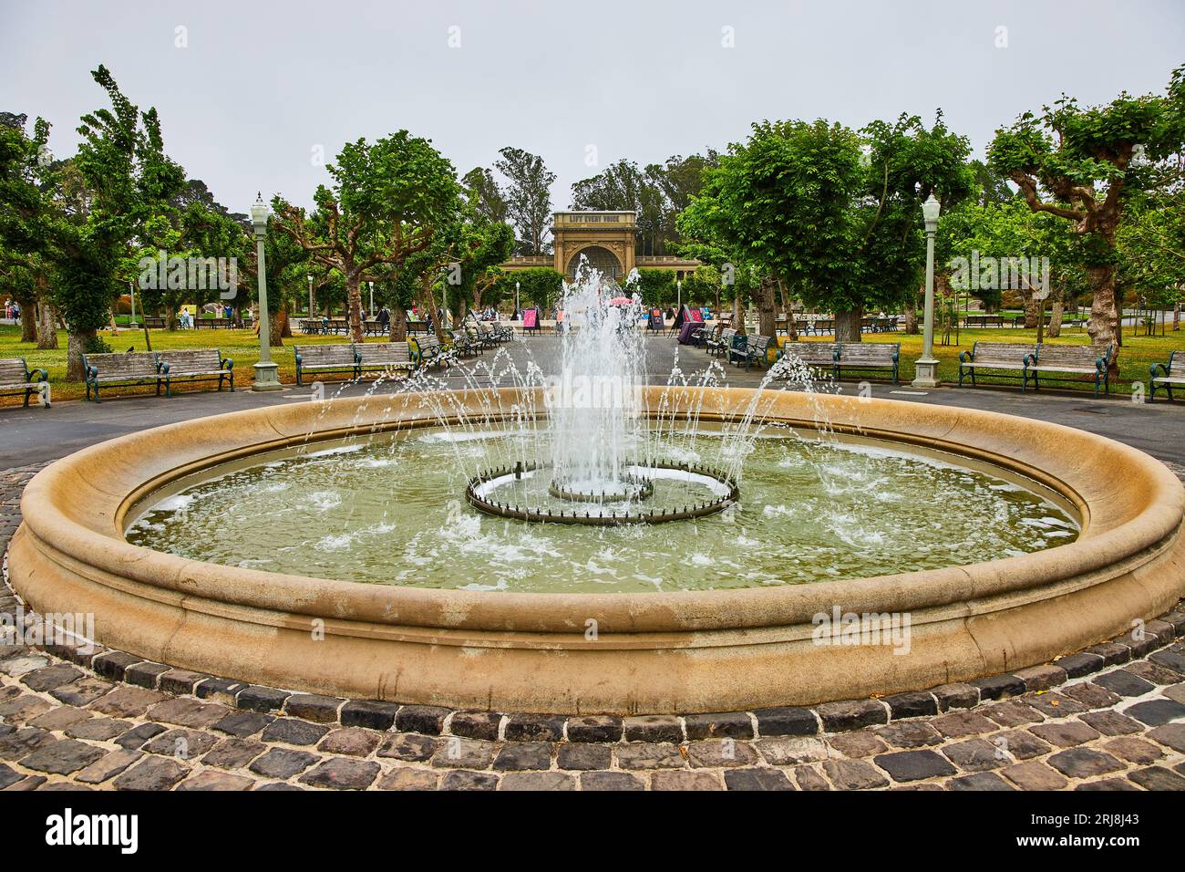Water fountain with benches around circular pathway and park in ...