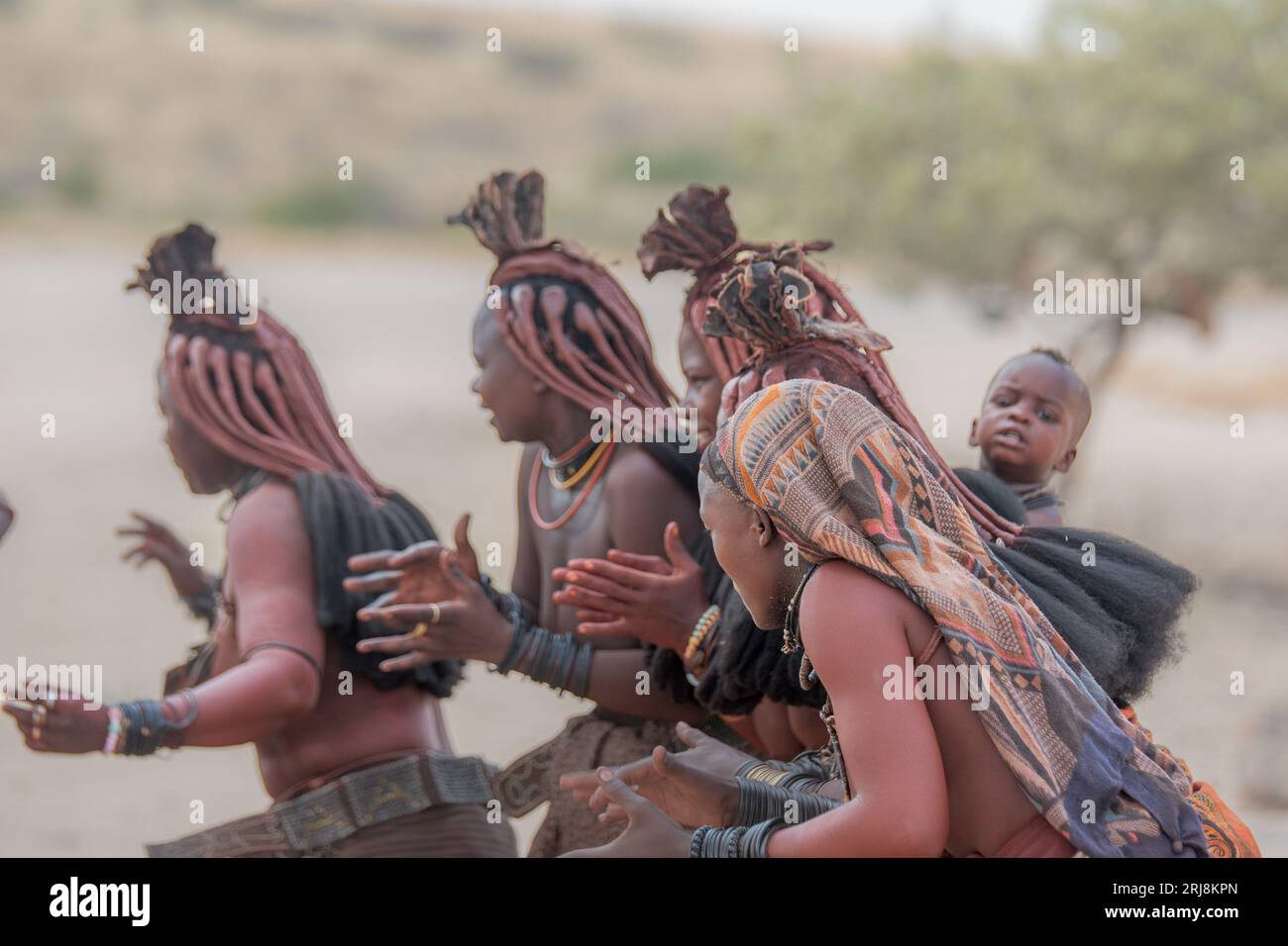 A group of Himba women in traditional attire running through a sandy ...