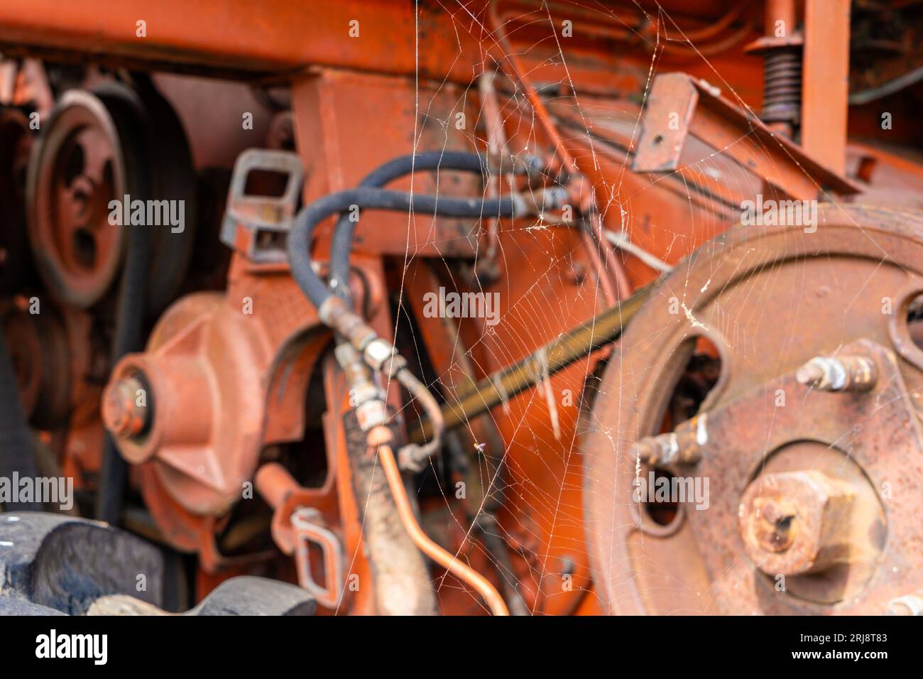 Abandoned red agriculture machine with pulleys and hydraulics covered ...
