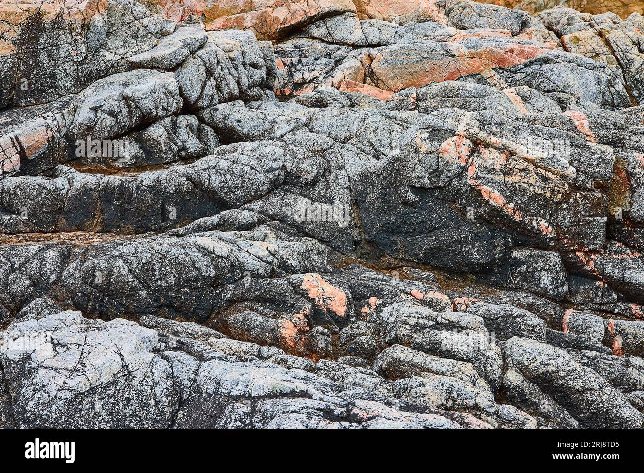 Light and dark grey stony cliff wall with tan rock and cracks in stone ...