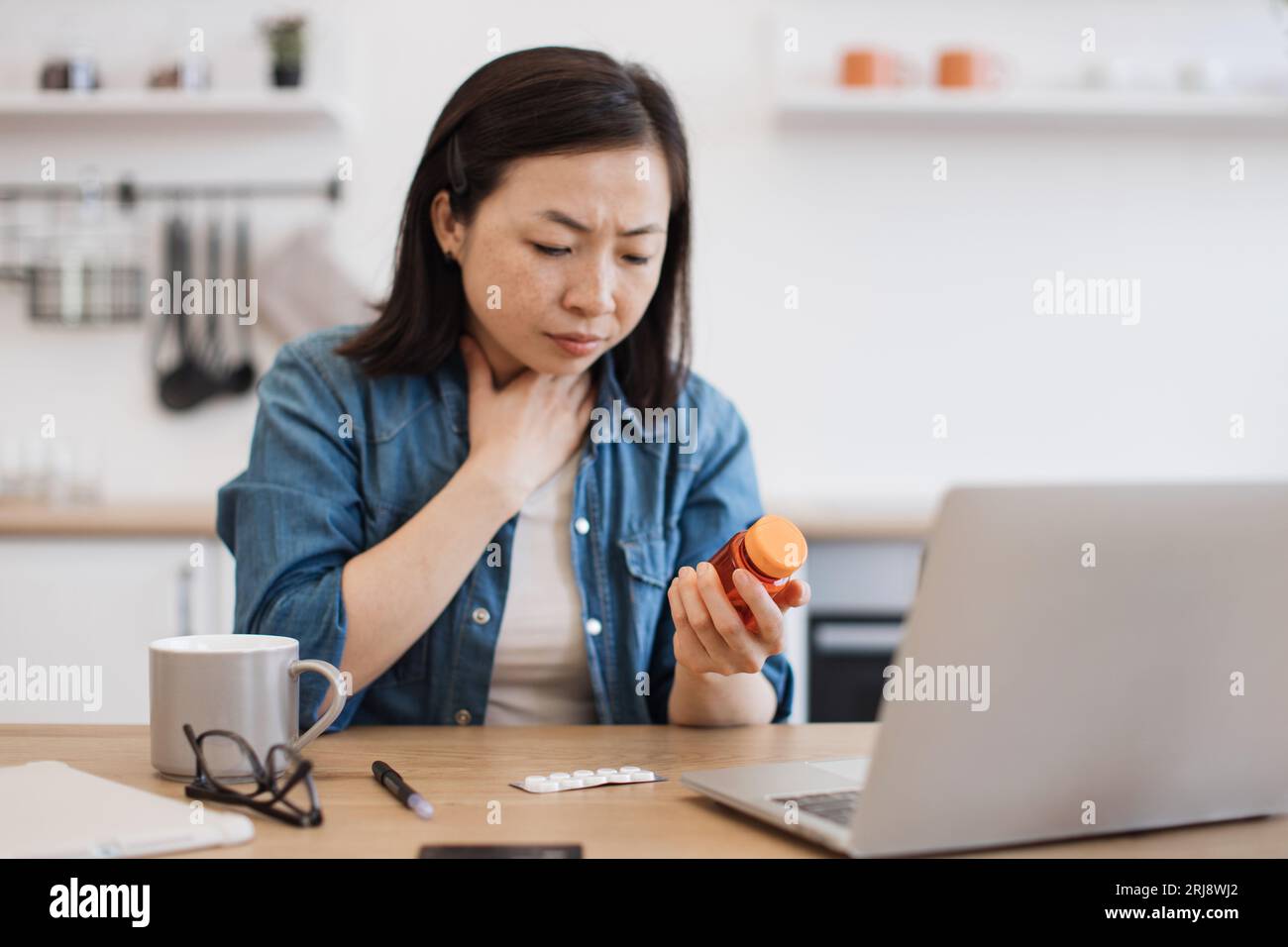 Young asian woman with sore throat holding pill bottle during online ...