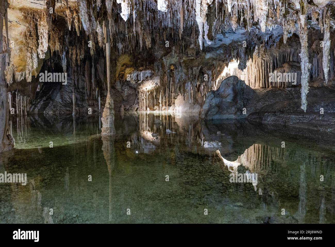 Underground pool with calm reflections with stalactites hanging from ...