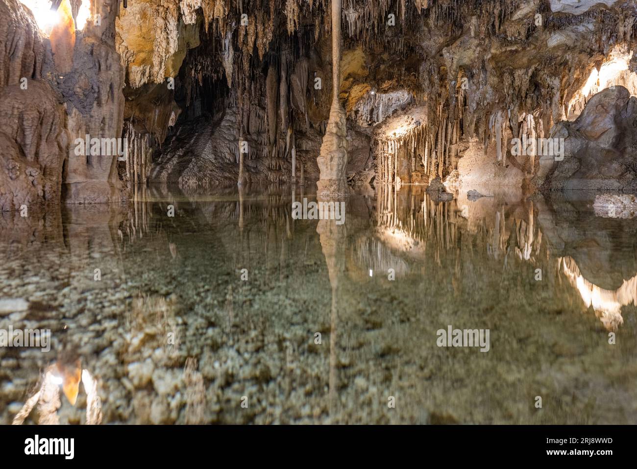 Underground pool with calm reflections with stalactites hanging from ...