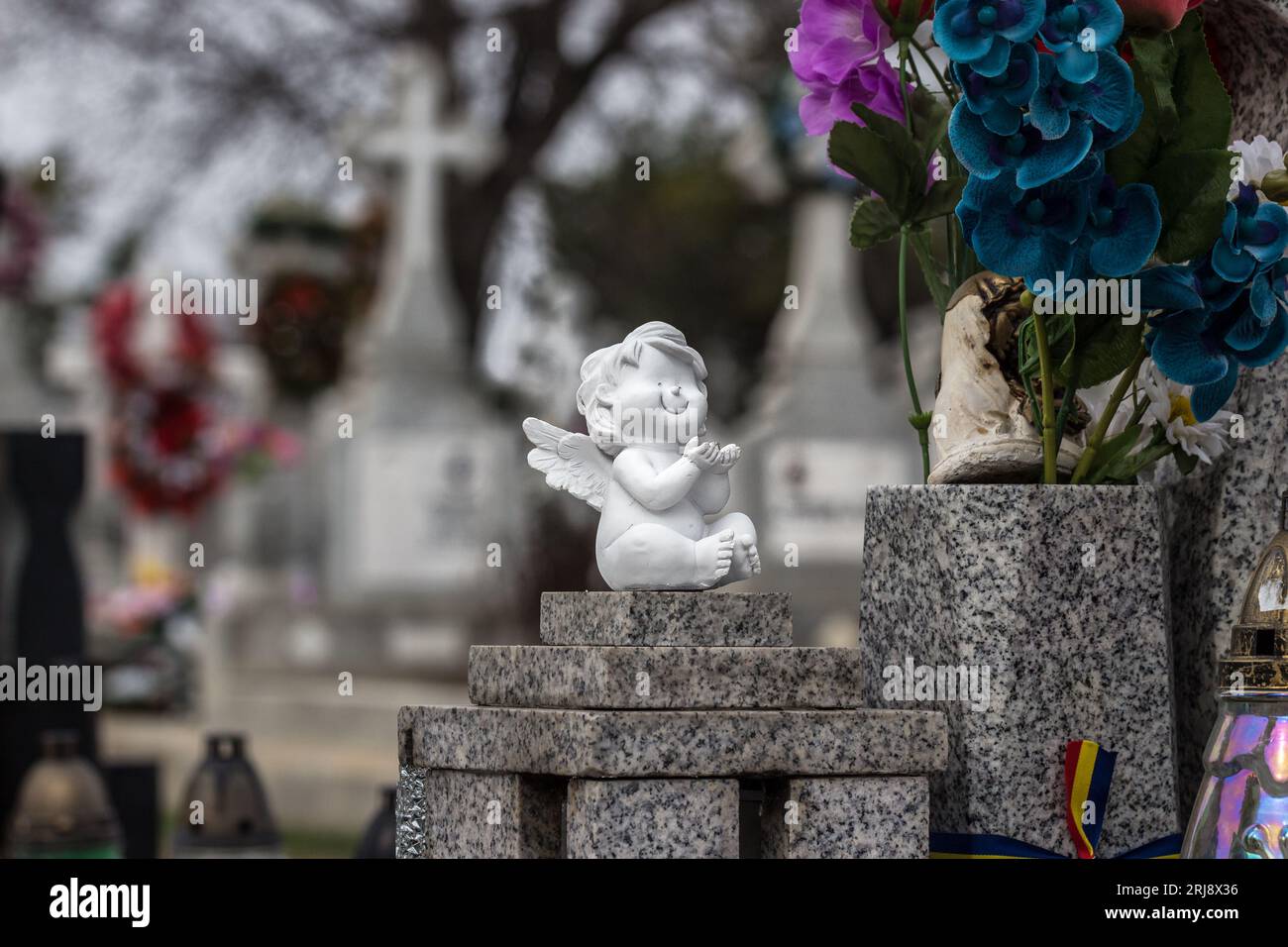 A stoic stone statue stands at the entrance of a cemetery, adorned with ...