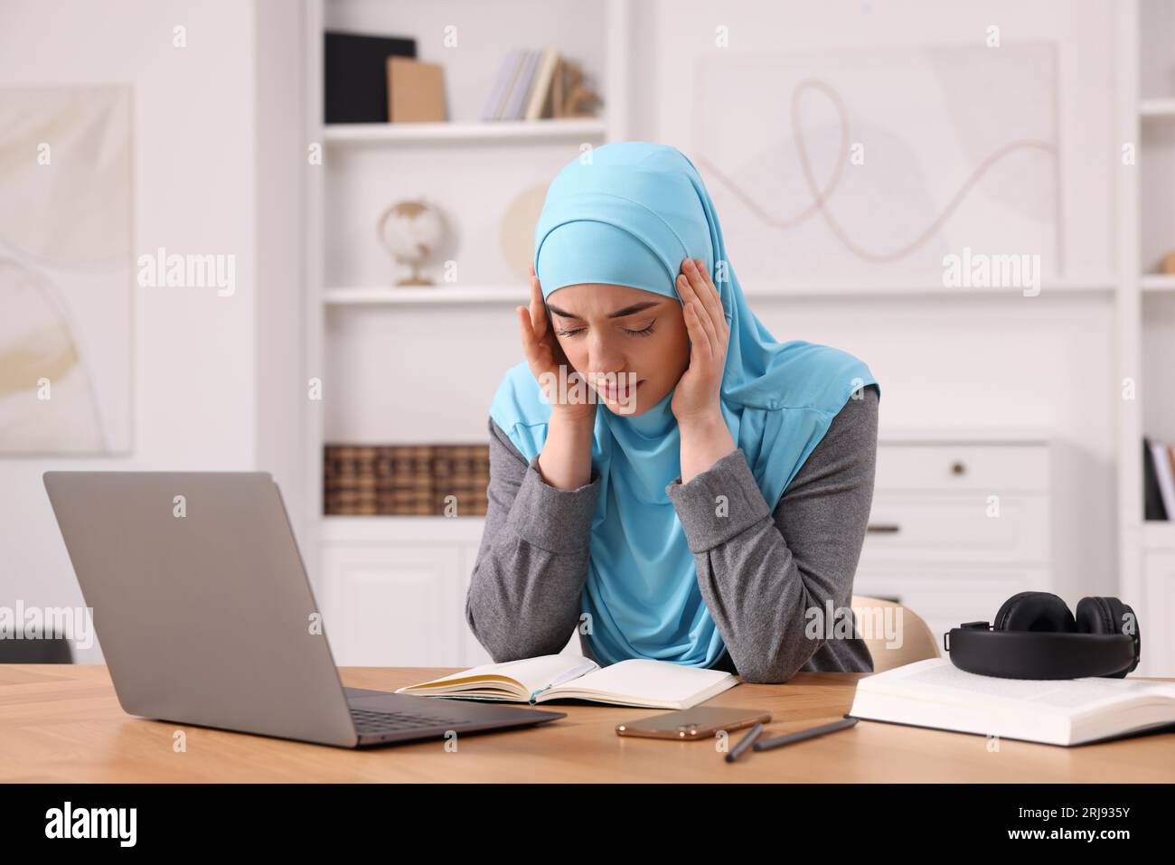 Tired Muslim woman working near laptop at wooden table in room Stock ...