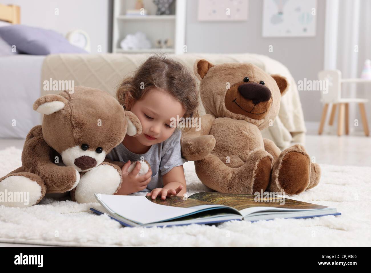 Cute little girl reading book near teddy bears on floor at home Stock ...