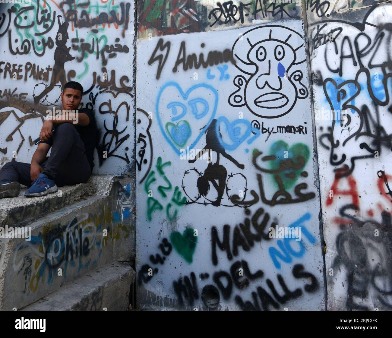 A Palestinian young man sitting by the Israeli security barrier in ...