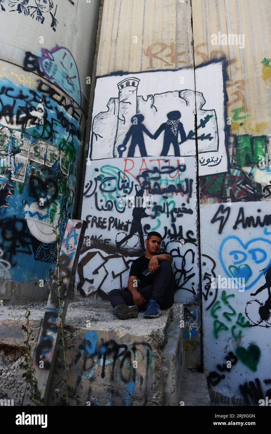 A Palestinian young man sitting by the Israeli security barrier in ...