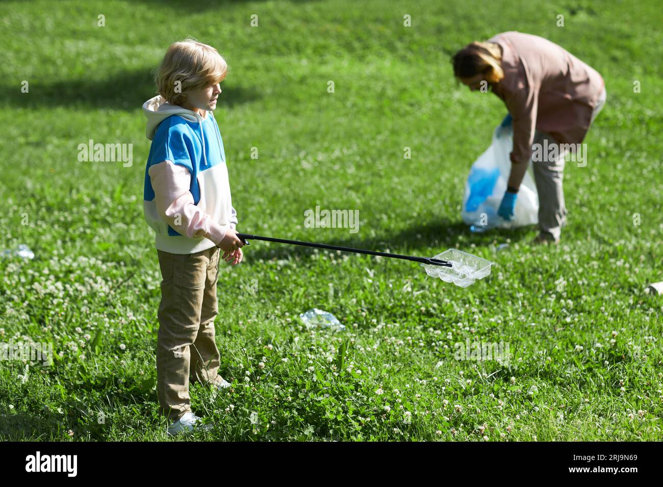 High angle portrait of blond boy picking up trash in nature standing on ...