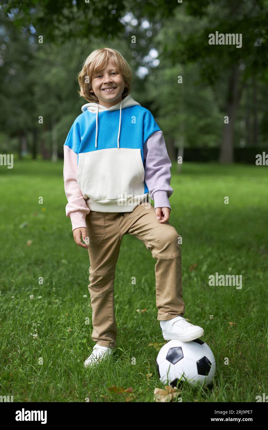 Vertical full length portrait of blonde tween boy playing football in ...