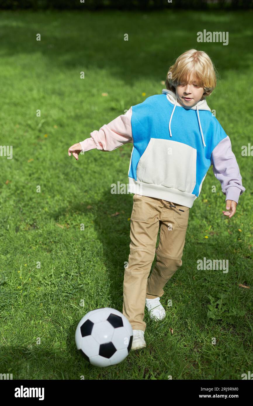 Vertical portrait of active tween boy playing football on green grass ...