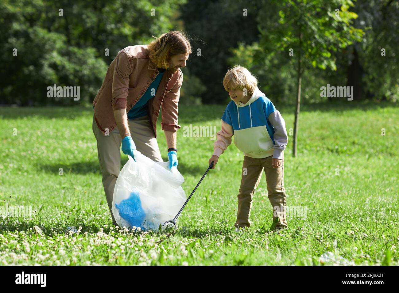 Full length portrait of father and son picking up trash in nature ...