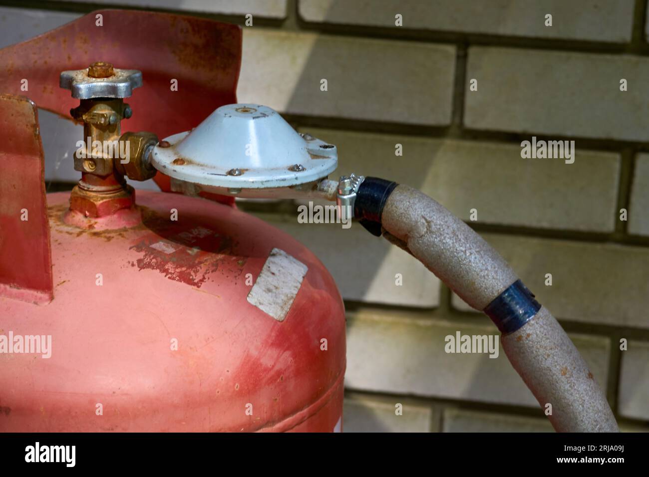 Connected metal gas cylinder against a white brick wall in a country ...