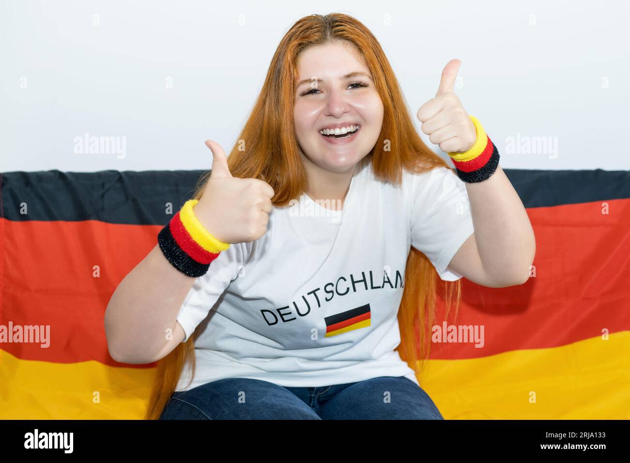 Beautiful german female soccer fan with flag of Germany indoors at home ...