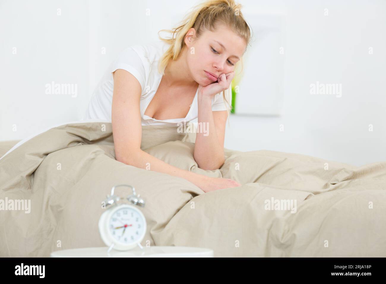 woman in bed looking miserably at alarm clock Stock Photo - Alamy
