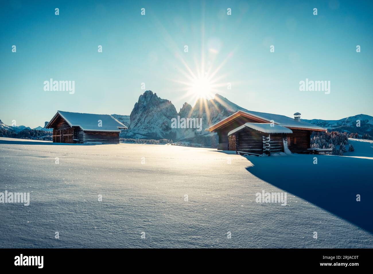 Small wooden log cabins on snowy meadow Alpe di Siusi on blue sky ...