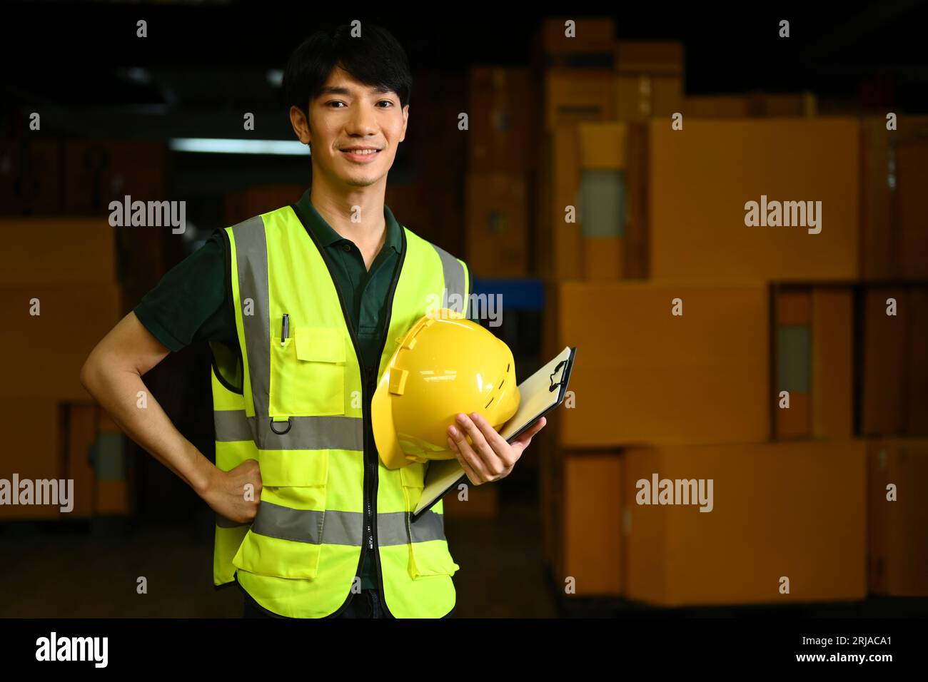 Handsome male warehouse worker holding hard hat standing near stack of ...