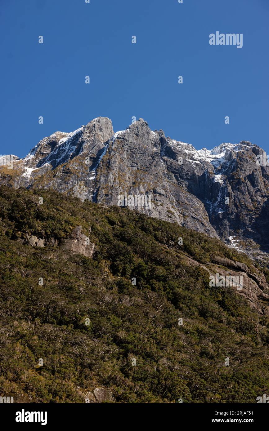An image of a rocky cliffside with snow on it's peak. In the foreground ...