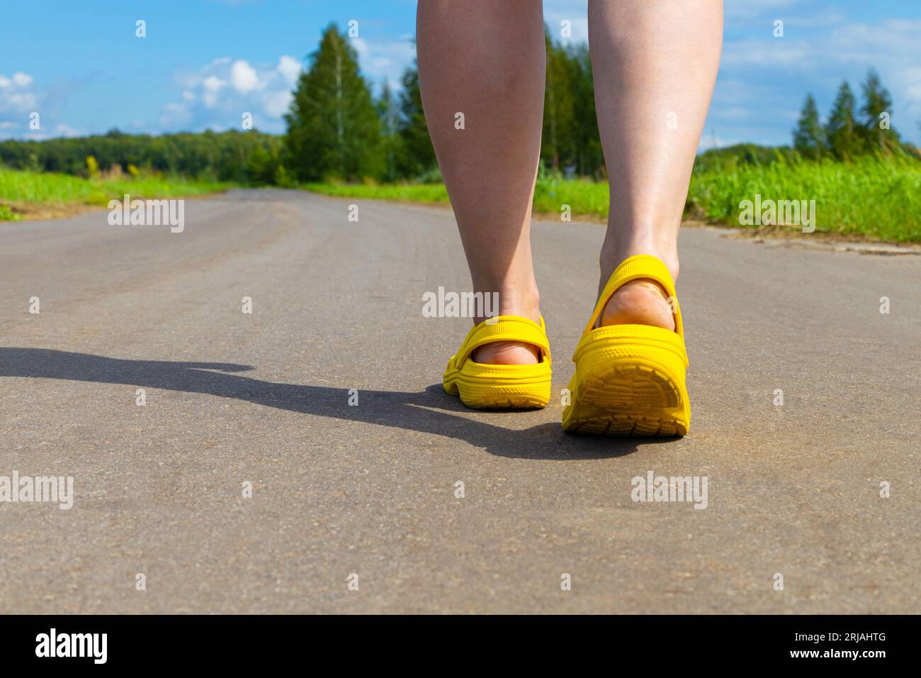 a man walks along an empty road in summer shoes. feet on the background ...