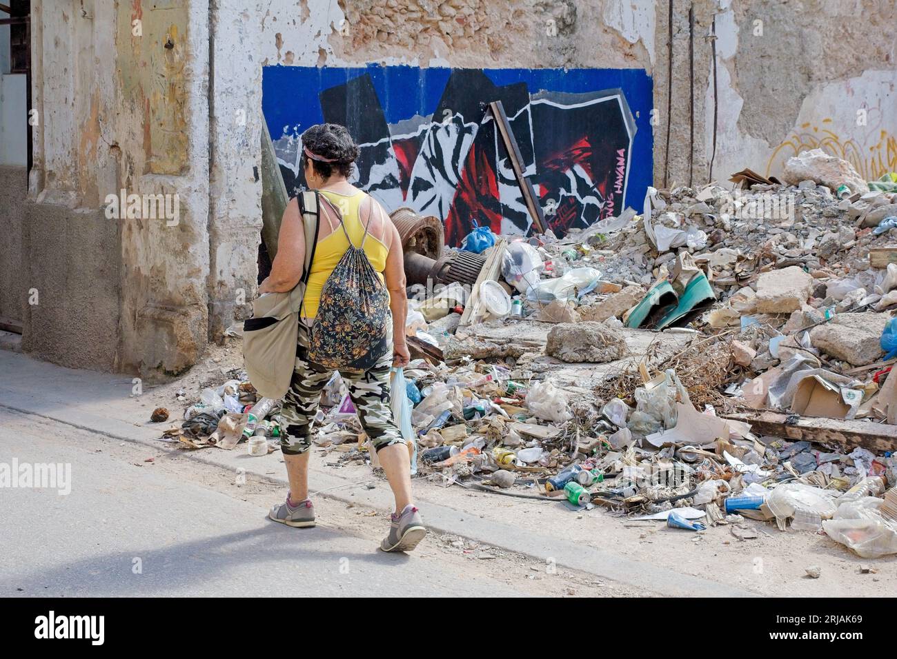 Havana, Cuba, a person carrying bags walk by a garbage dump in a city ...