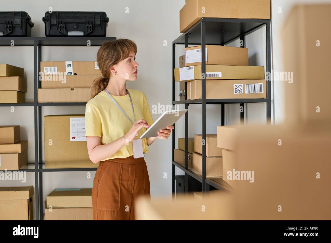 Young female manager with tablet standing in front of tall rack with ...