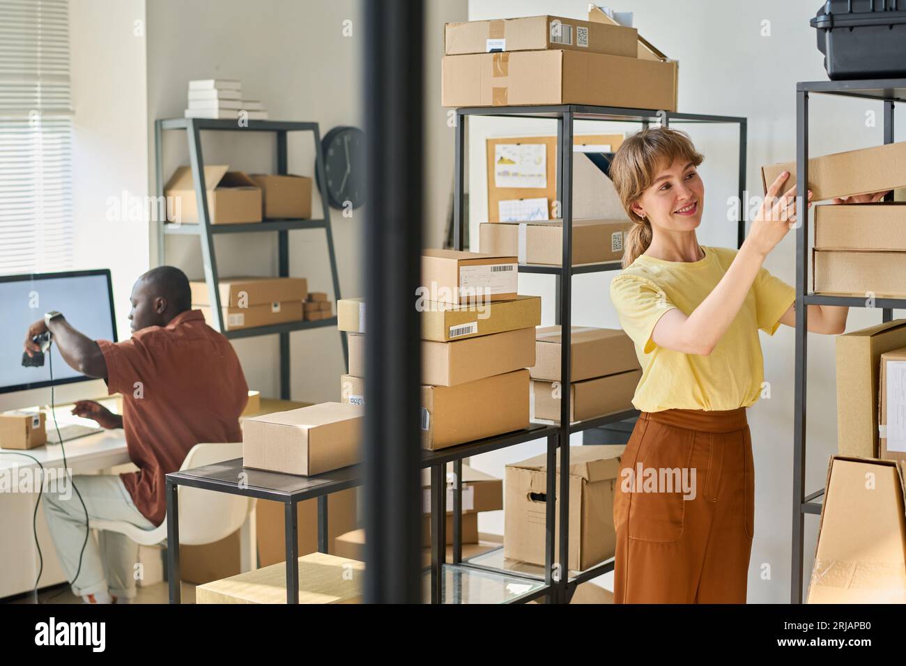 Happy young woman standing by rack against male colleague scanning ...
