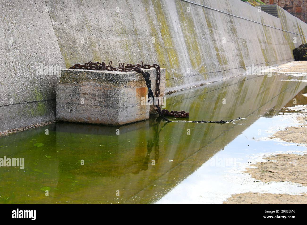 Concrete block with rusty chain on a puddle of green water with ...