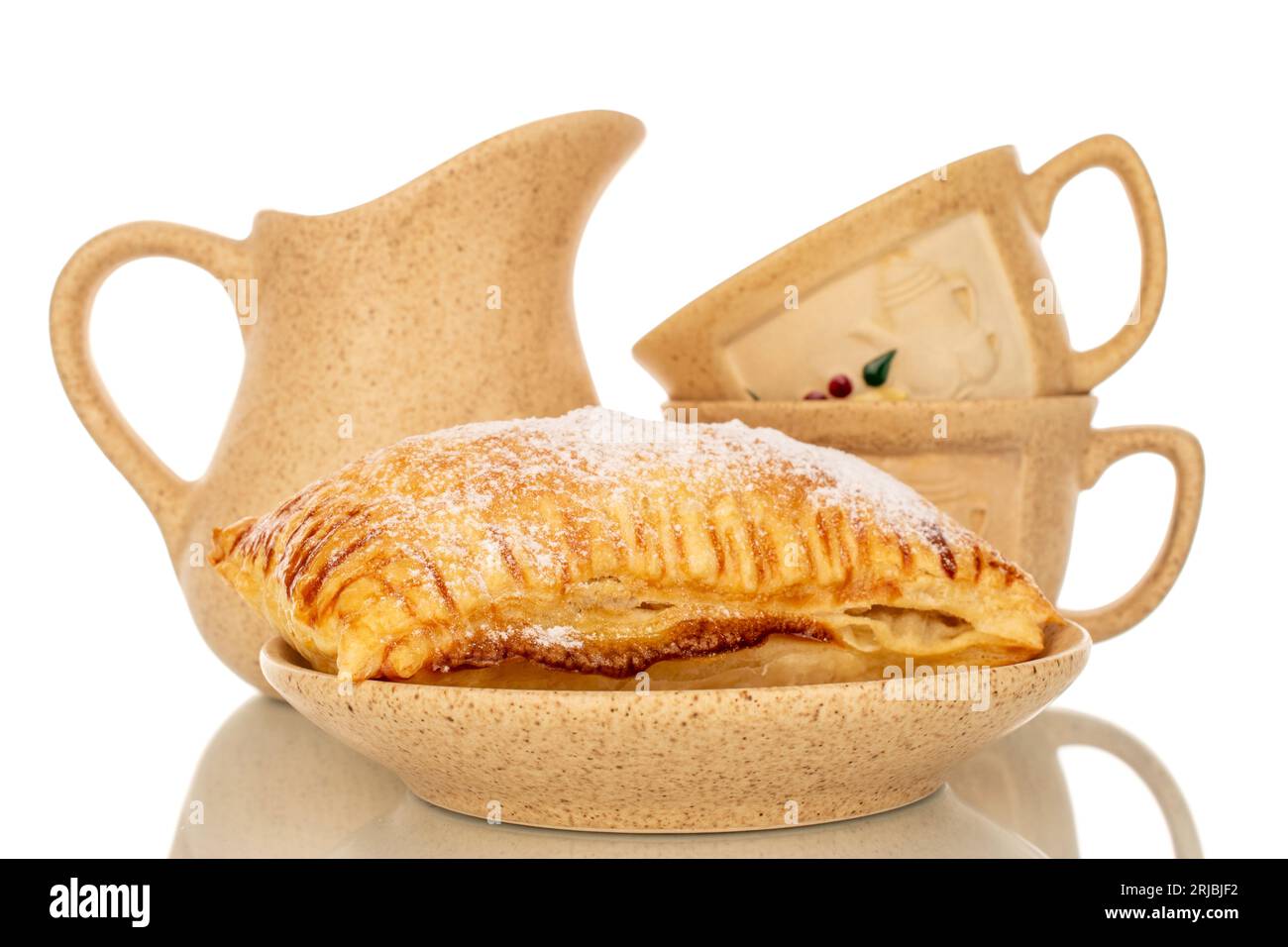 One aromatic puff pastry bun with apples on a clay plate with two cups ...