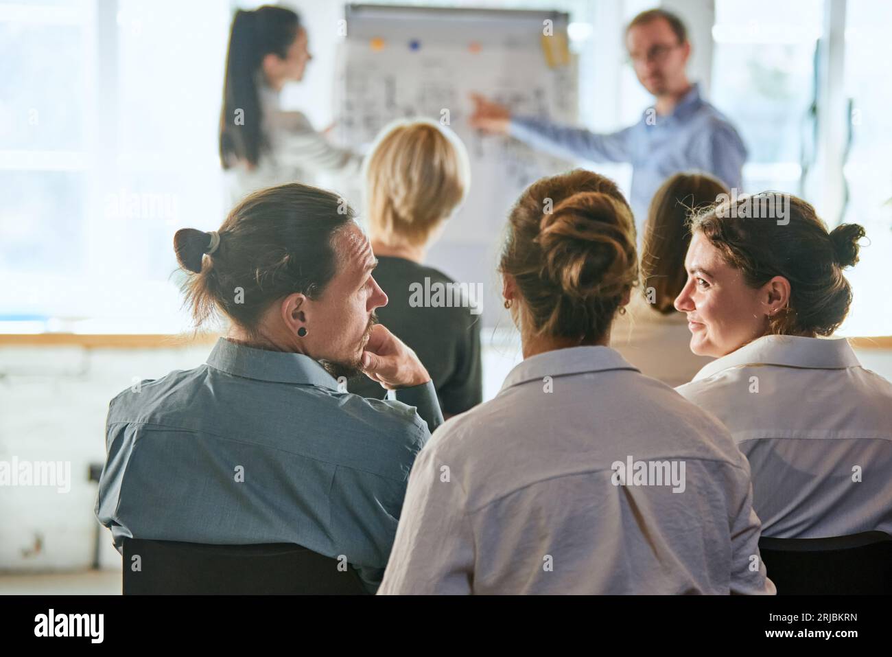 Male and female creative leaders give presentation to group of office ...