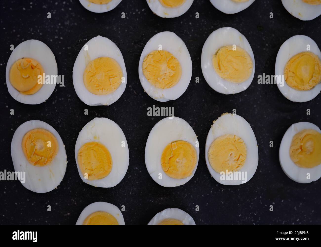 Hard boiled eggs cut in half on black background Stock Photo - Alamy