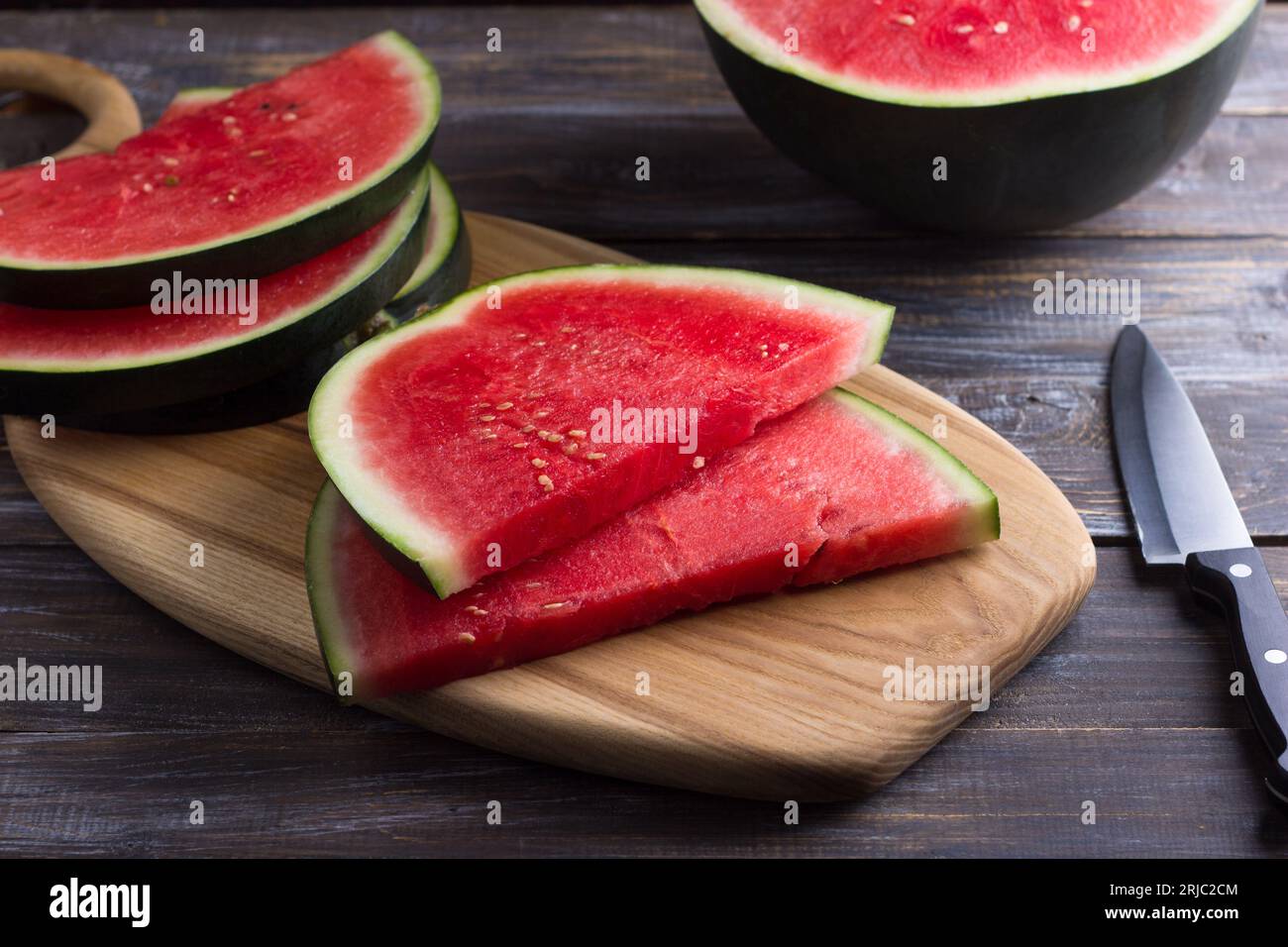 Seedless watermelon, slices on a wooden board with a knife and half of ...