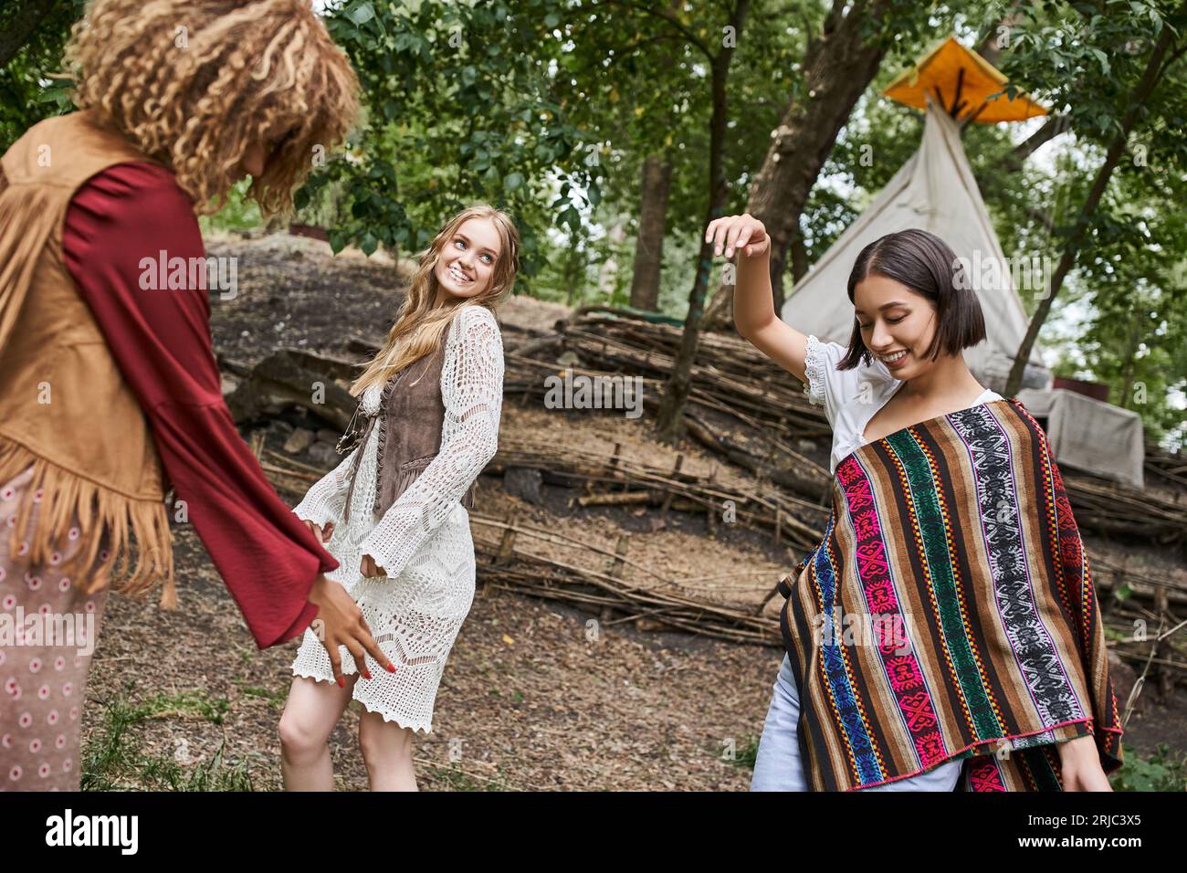 young and interracial girlfriends in boho outfits dancing on lawn in ...