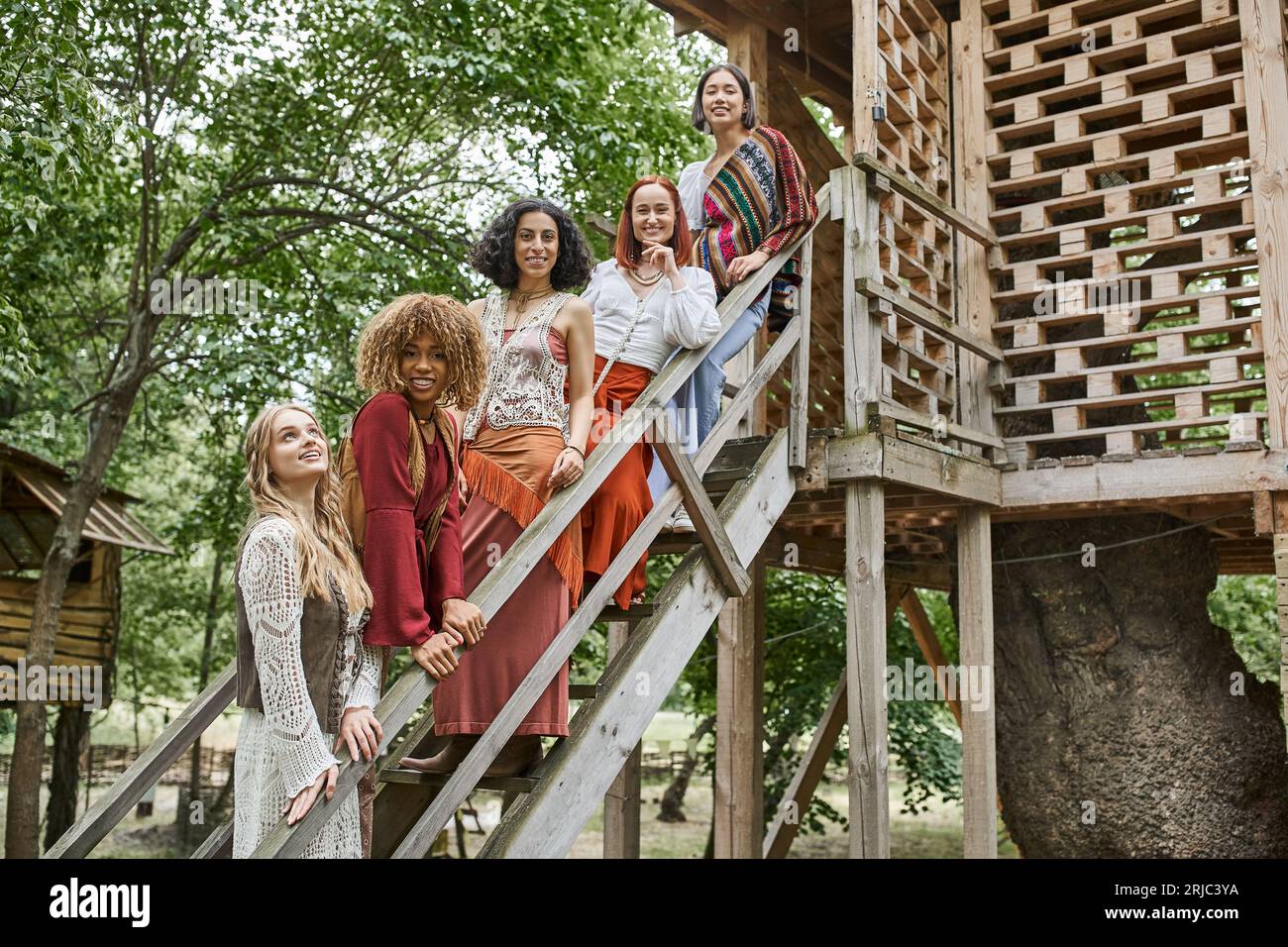 happy multiethnic girlfriends in trendy boho style clothes standing on ...