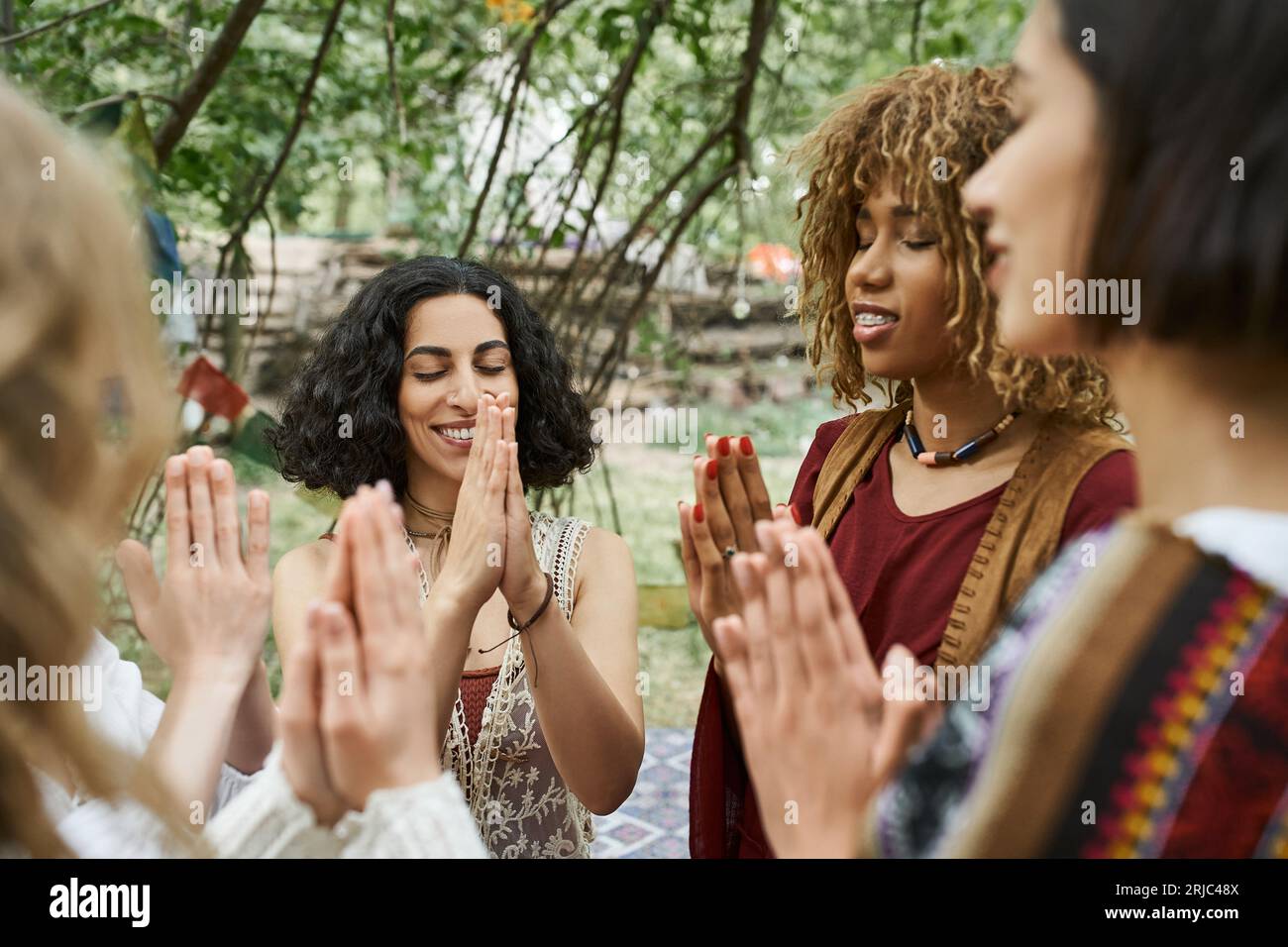 smiling and stylish interracial women praying together outdoors in ...