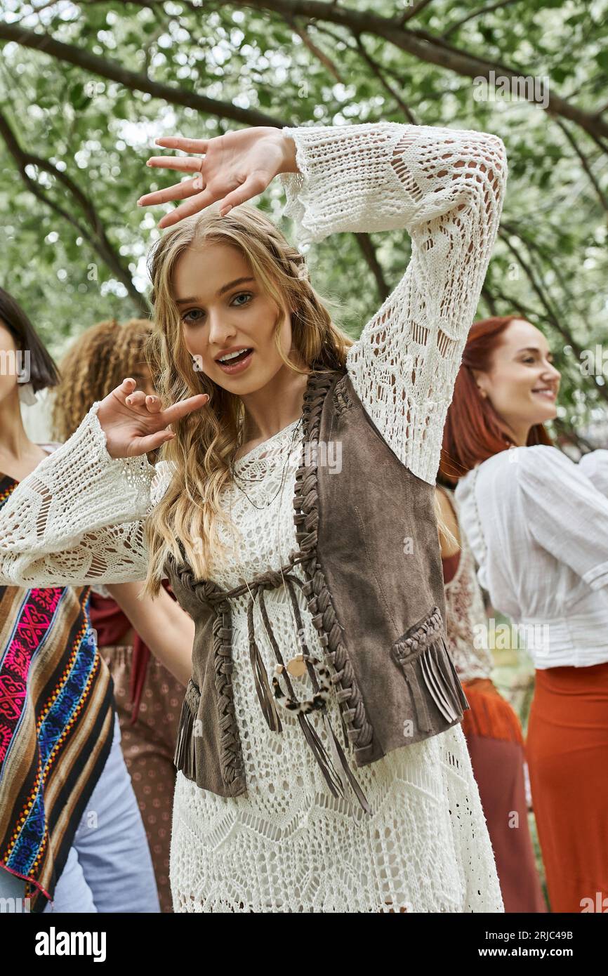 Young blonde woman in boho outfit looking at camera and dancing near ...