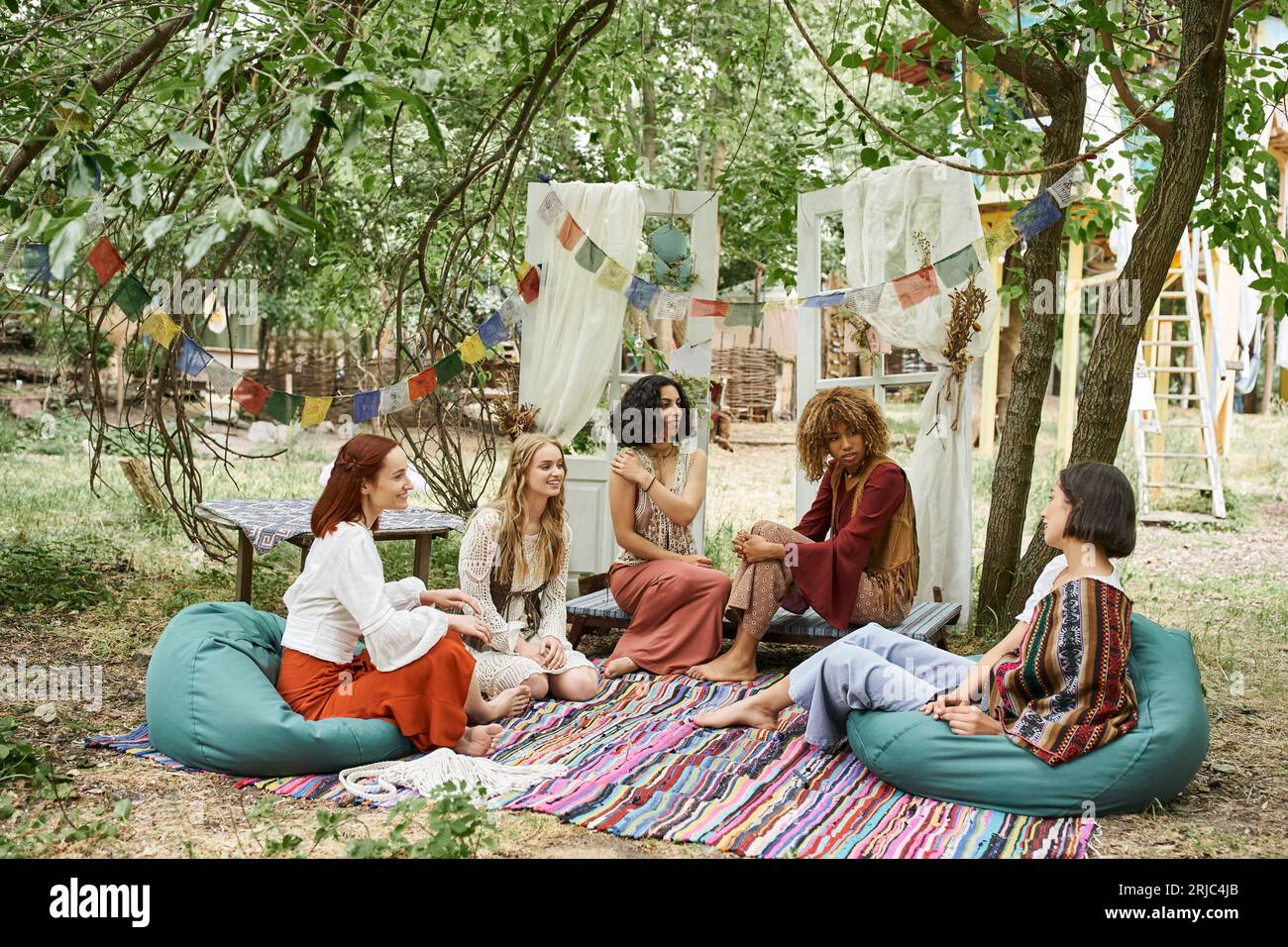 boho style multiethnic girlfriends talking in park of retreat center ...