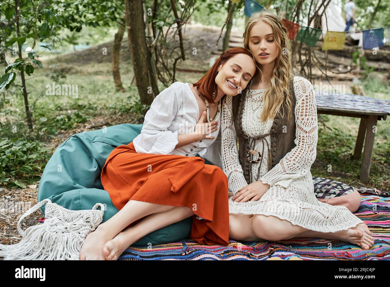 positive women in stylish boho outfits meditating together on meadow in ...